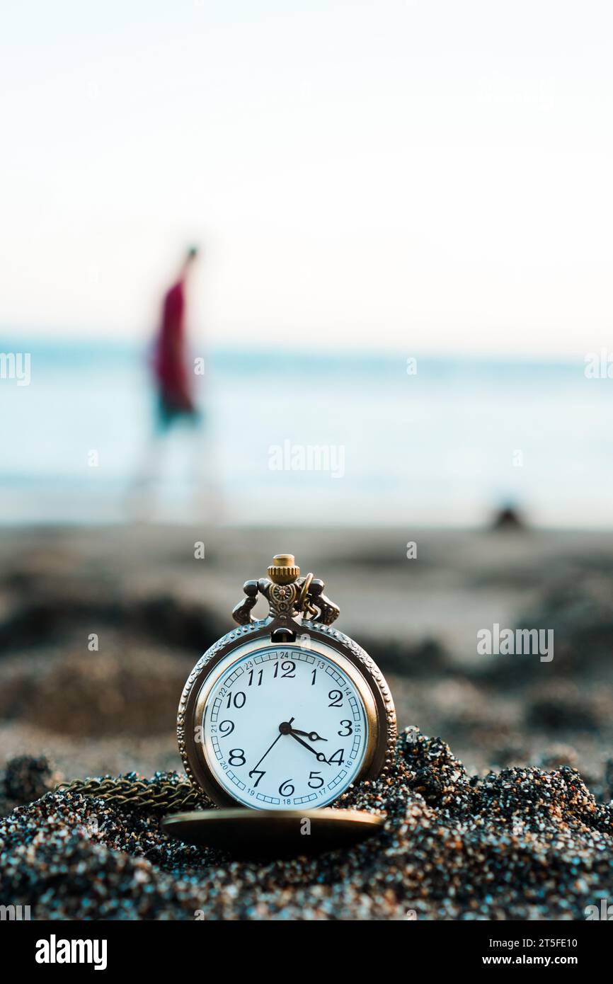 Gold pocket watch lies on a sandy beach with a person walking on the ...
