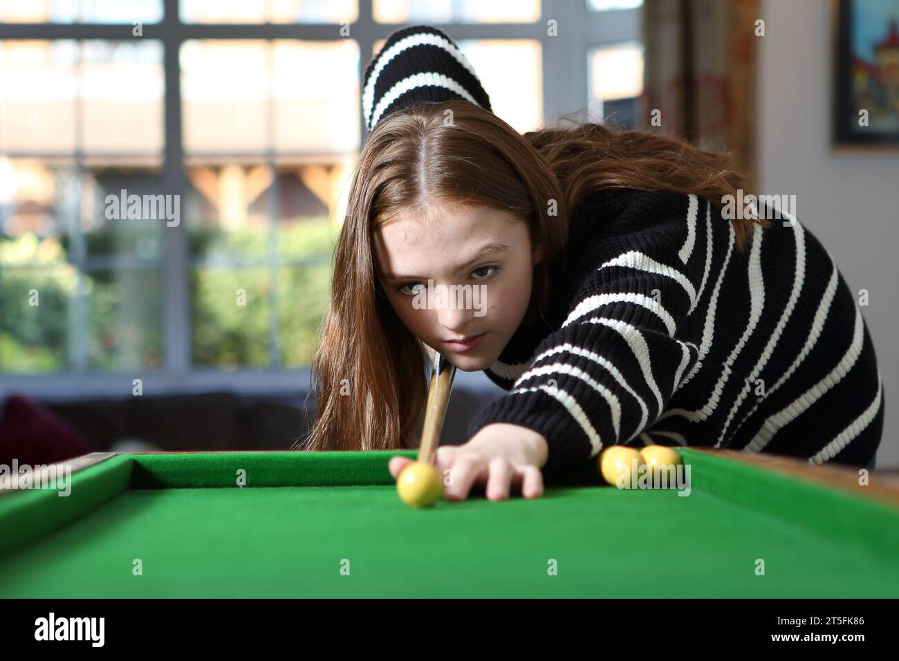 Teen girl playing traditional pub game of bagatelle in lounge at home ...
