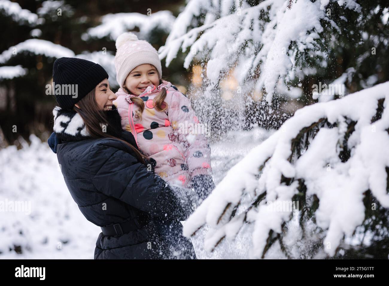 Happy mom and daughter shake off the snow from a Christmas tree branch ...