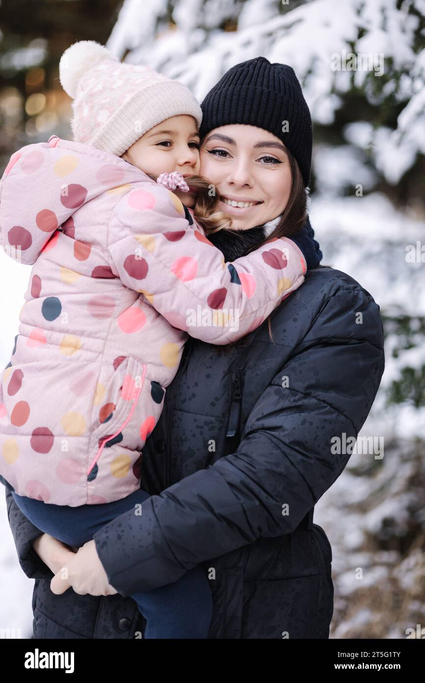 Beautiful young mom hug her adorable little daughter in snowy forest. Happy family Stock Photo ...