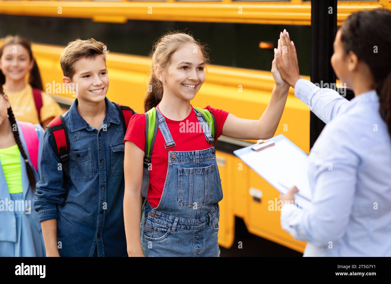 Black teacher lady giving high-fives to kids boarding the school bus ...