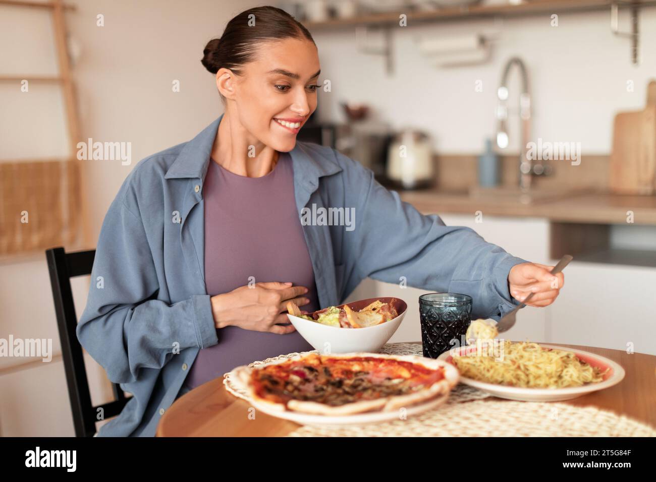 Hungry pregnant woman relishing meal at her cozy kitchen Stock Photo ...