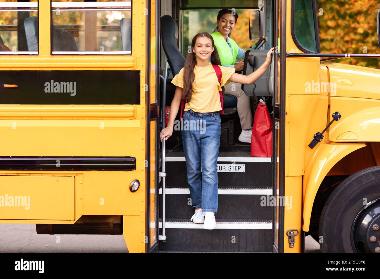 Happy preteen girl getting of the yellow school bus, smiling at camera ...