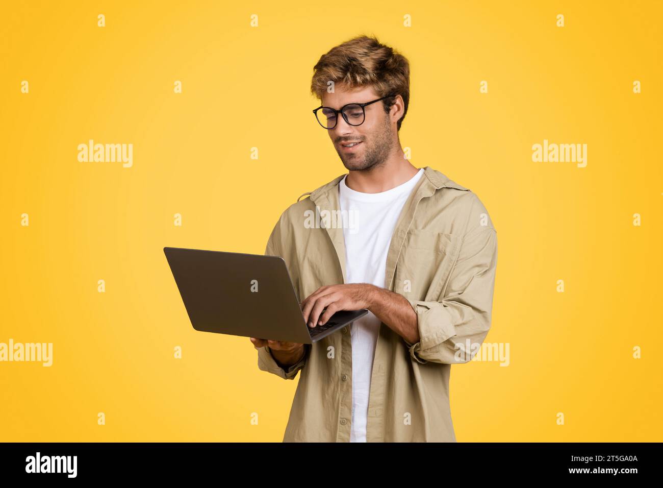 European man typing on laptop, standing against yellow background Stock ...