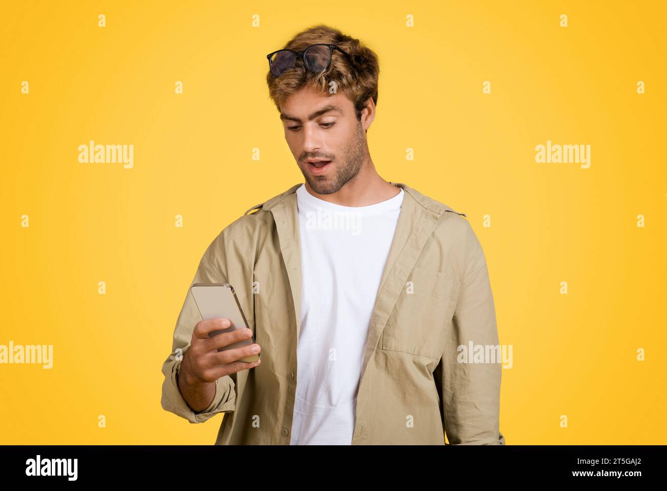 Shocked European man looking at cellphone screen on yellow background ...