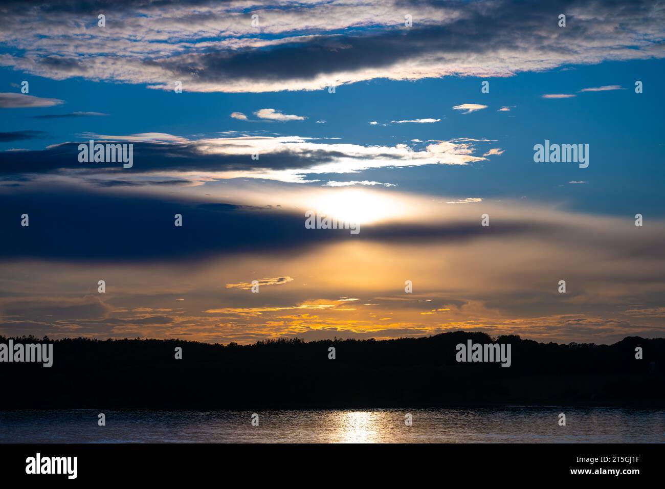 Sun setting behind hazy clouds in summer Stock Photo - Alamy