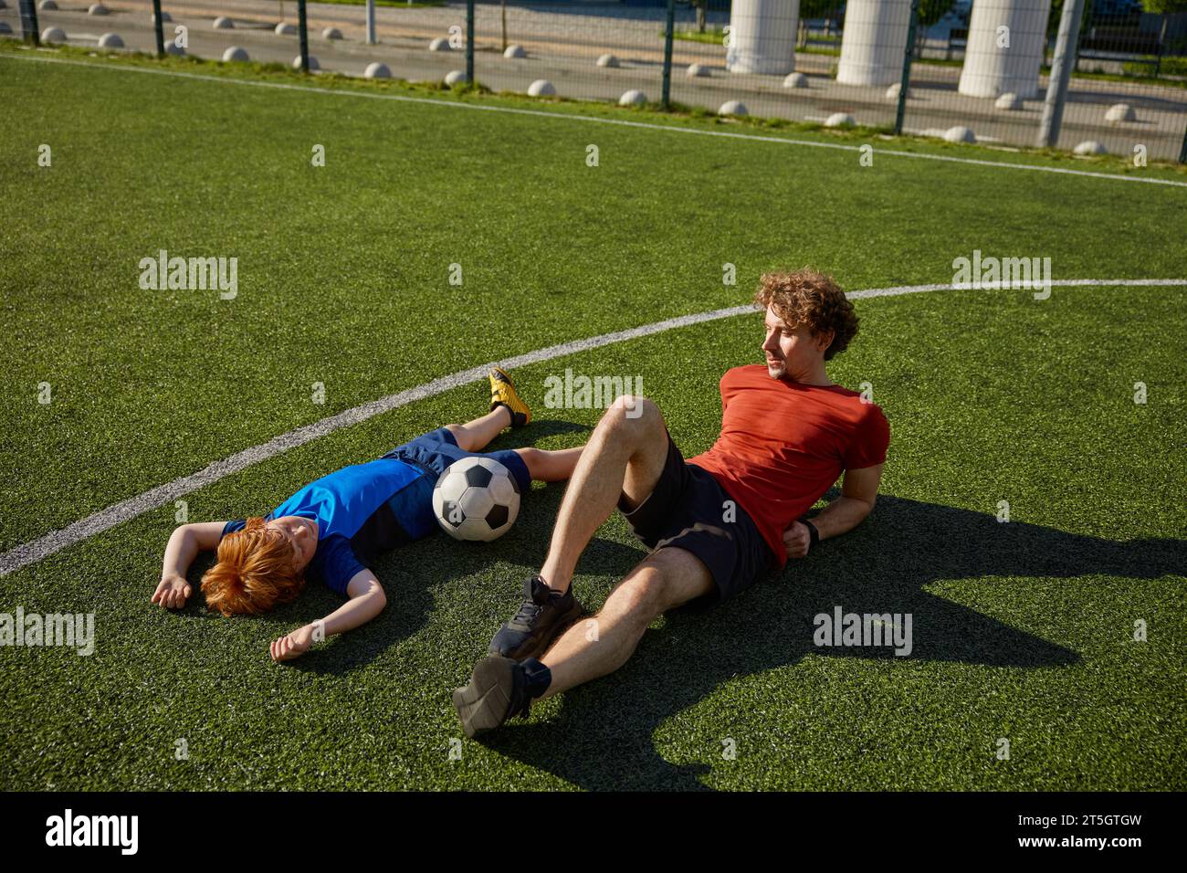Tired Father And Son Soccer Player Lying On Grass Of Football Field