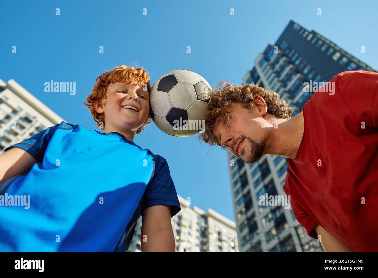 Closeup of adult man and boy child holding soccer ball between forehead ...