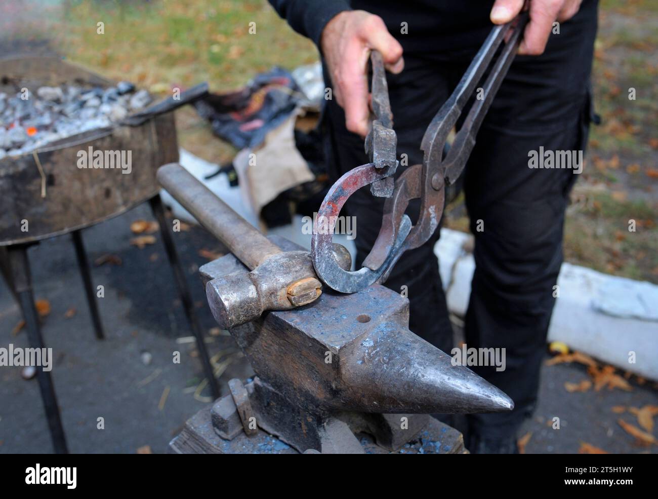 Blacksmith s hands holding forceps and a hammer forging a metal billet ...