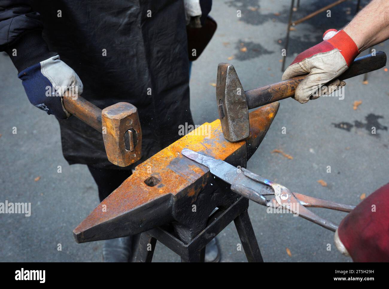 Blacksmith hands holding forceps and a hammer forging a metal billet ...