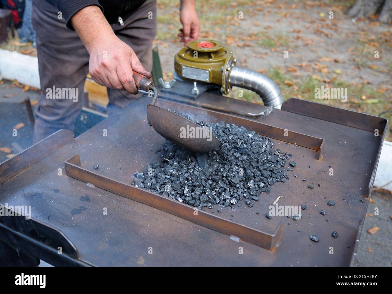 Blacksmith s hand adding coal to a burning forge with a scoop. At the ...