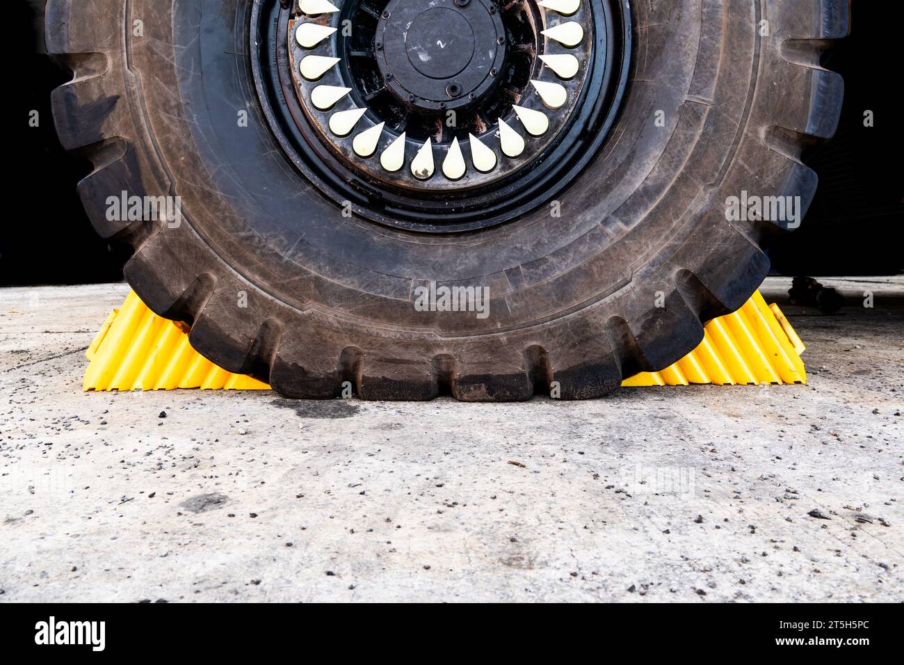 A pair of yellow heavy duty wheel chock wedged against a vehicle tyre ...