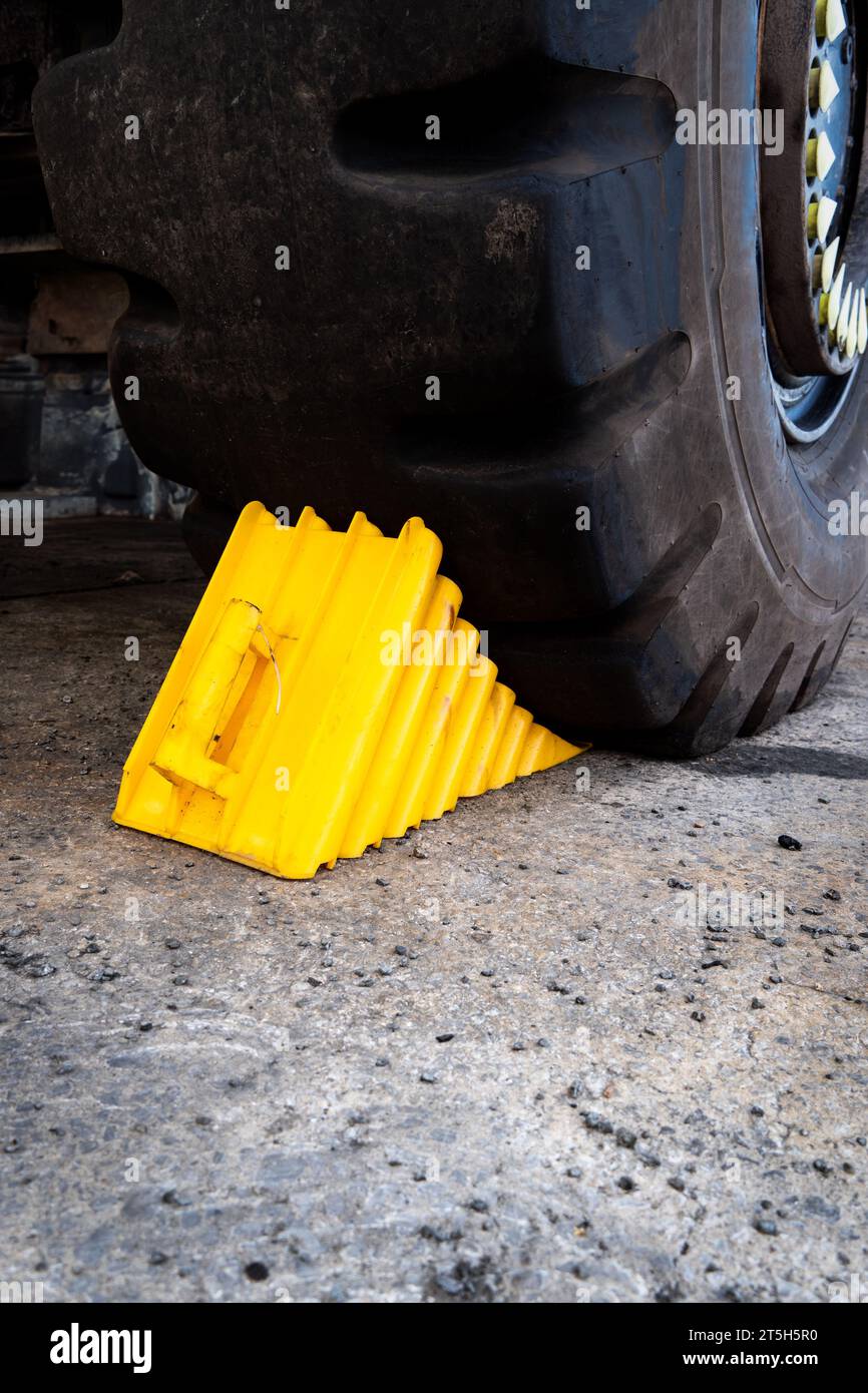 A yellow heavy duty wheel chock wedged against a vehicle tyre as a ...