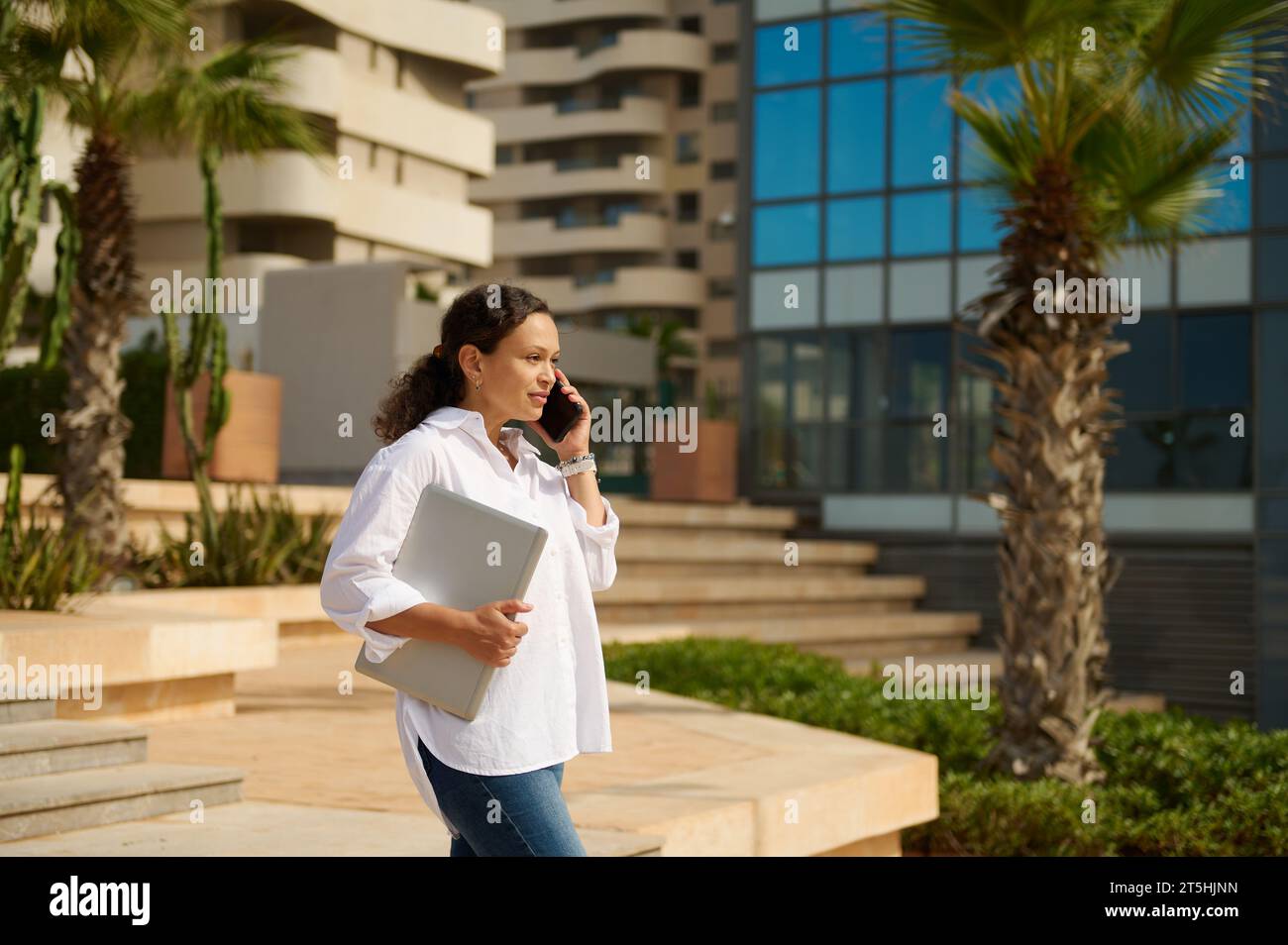 Confident multitasking woman entrepreneur talks on mobile phone, holds ...