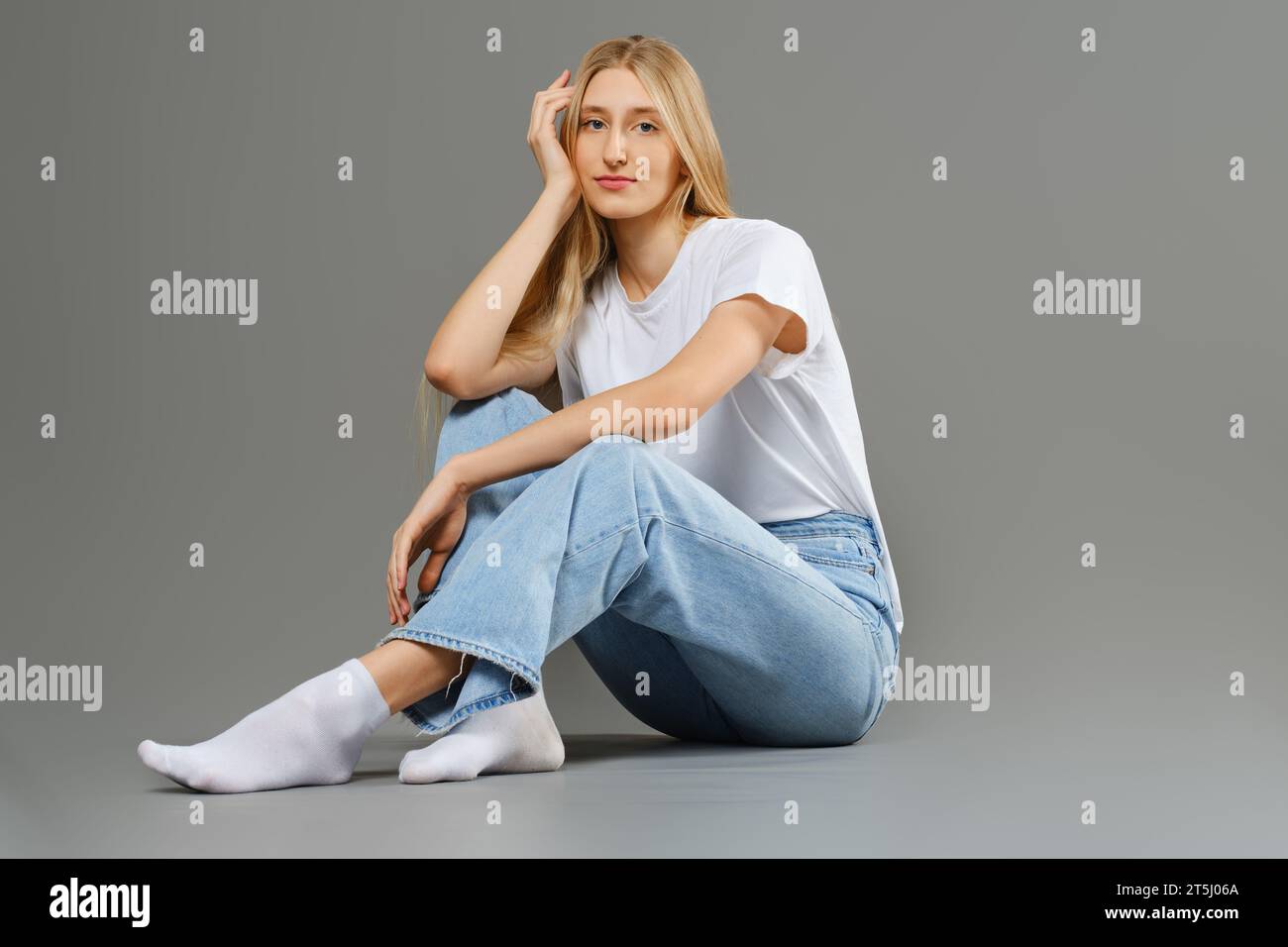 A bored woman sits on the floor with her head propped up on her hand ...