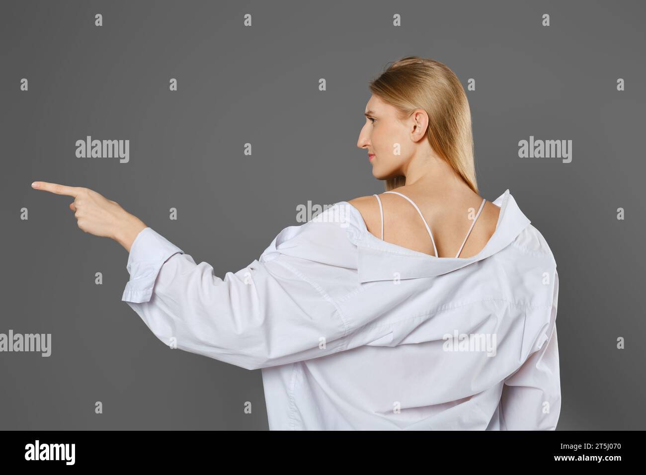 Back side view of woman wearing white shirt pointing to the side with ...