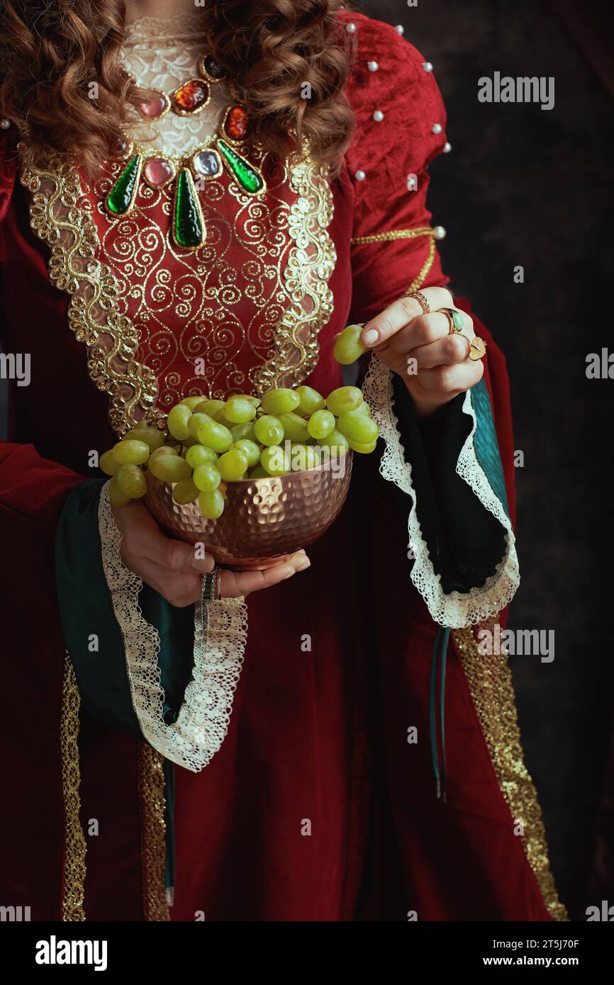 Closeup on medieval queen in red dress with plate of grapes on dark ...