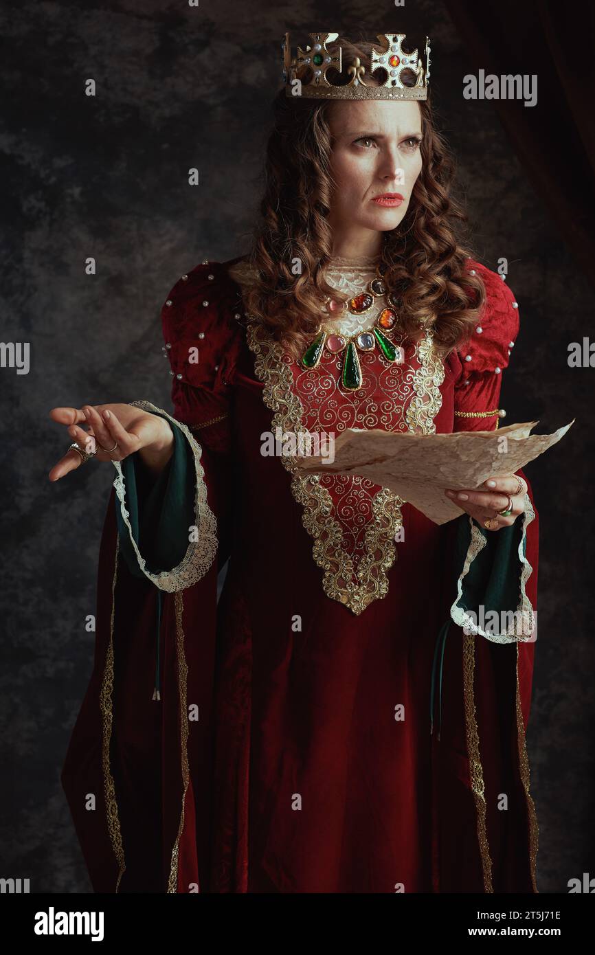 medieval queen in red dress with parchment and crown on dark gray ...
