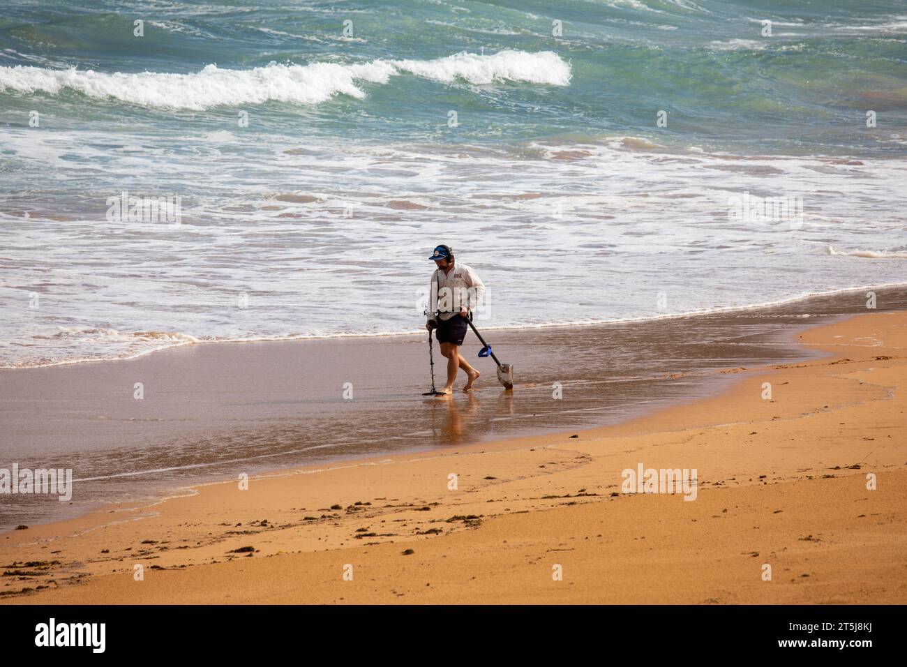 Sydney Australia man with a metal detecting device walks along a ...