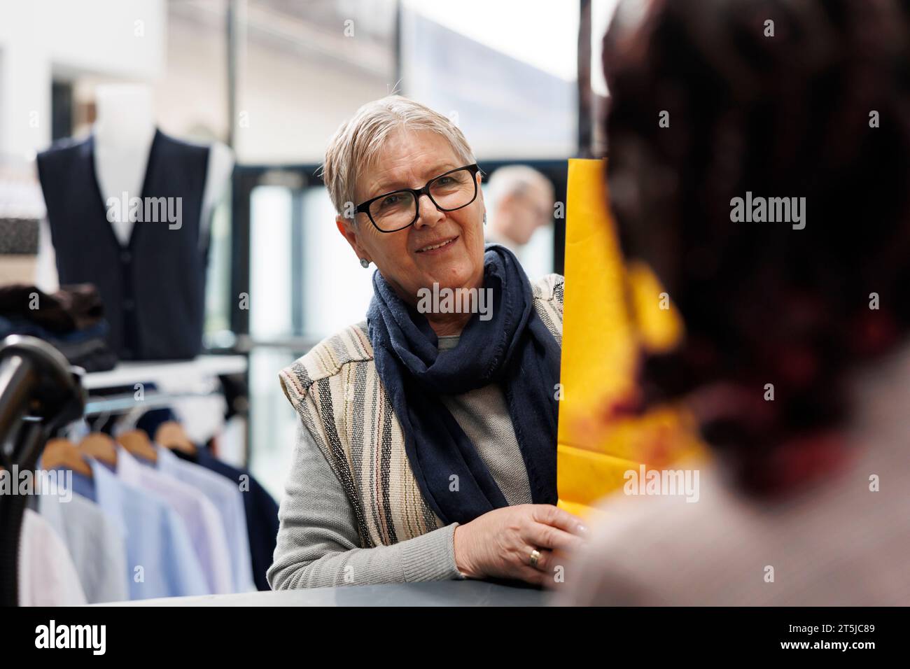 Elderly shopper taking shopping bags from employee, making purchase at ...