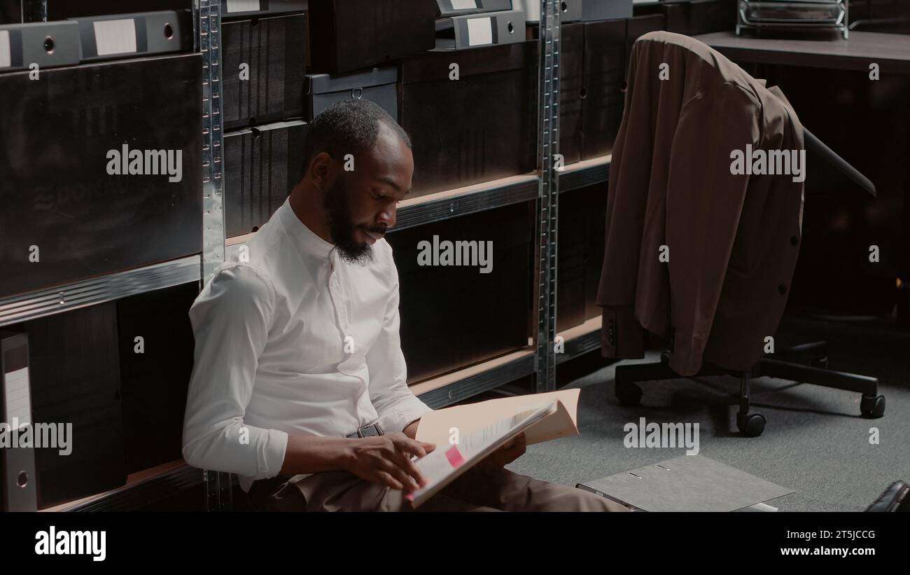 Police officer sitting on archive room floor with files conducting ...