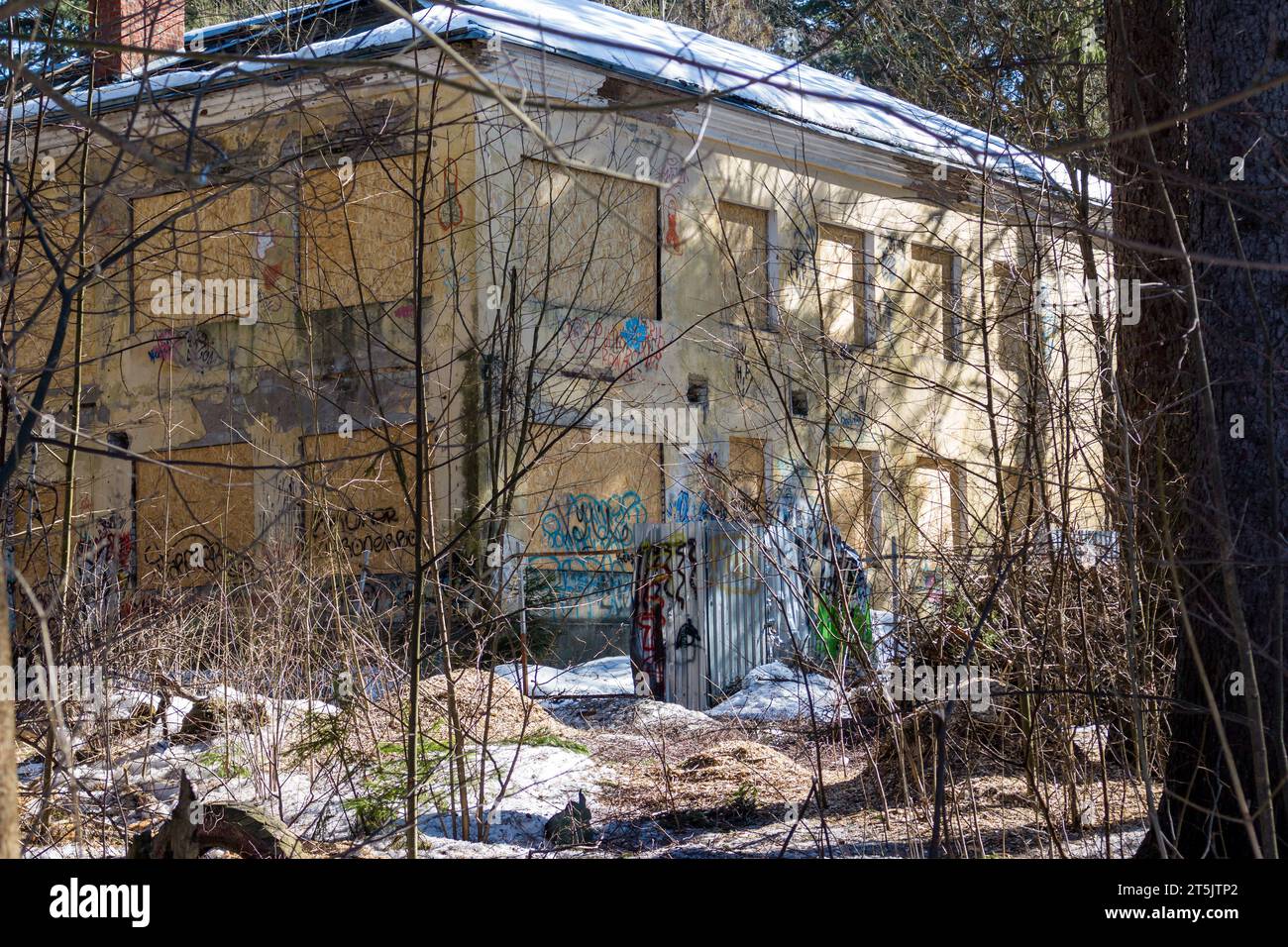 Two-story abandoned building with boarded up windows in a forest area ...