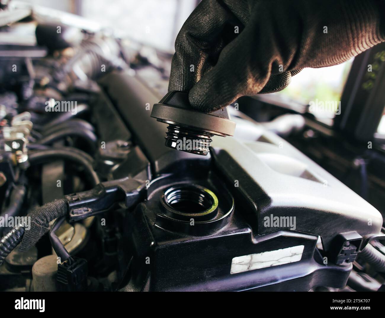 The hand of a car mechanic opens the engine oil cap to inspect before ...