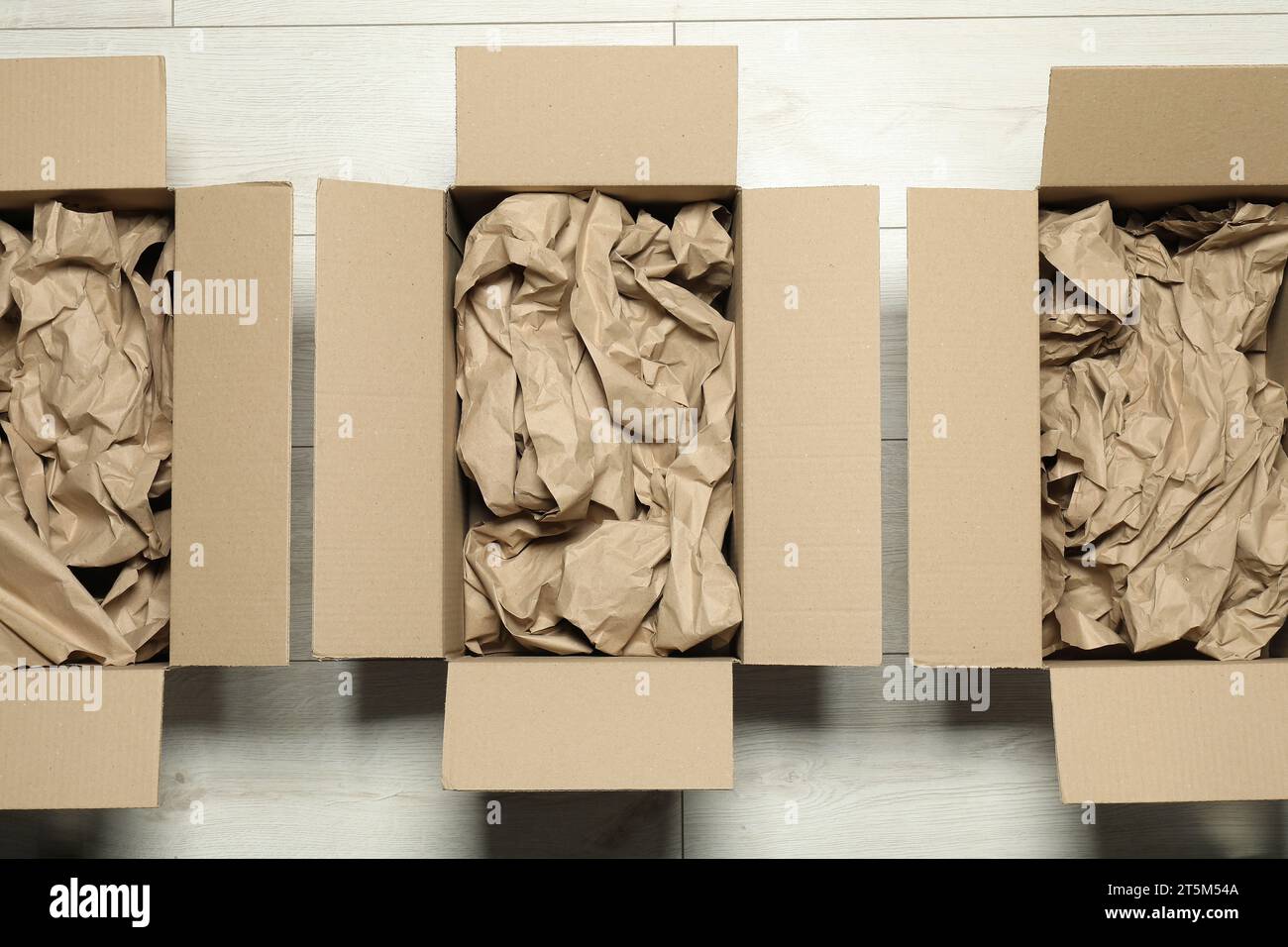 Open cardboard boxes with crumpled paper on white wooden floor, flat ...