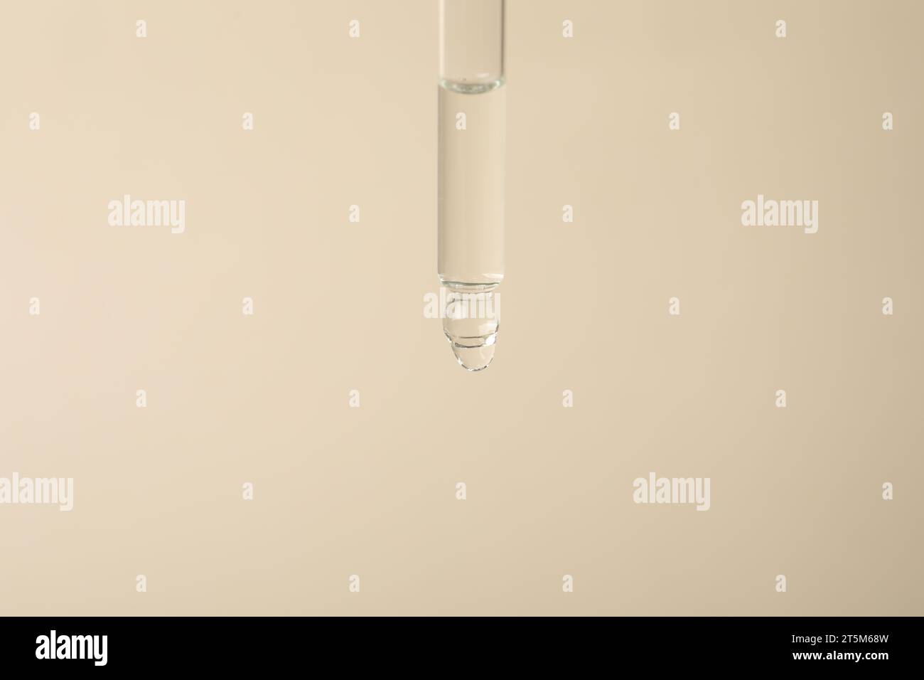 Dripping cosmetic serum from pipette on beige background, space for ...