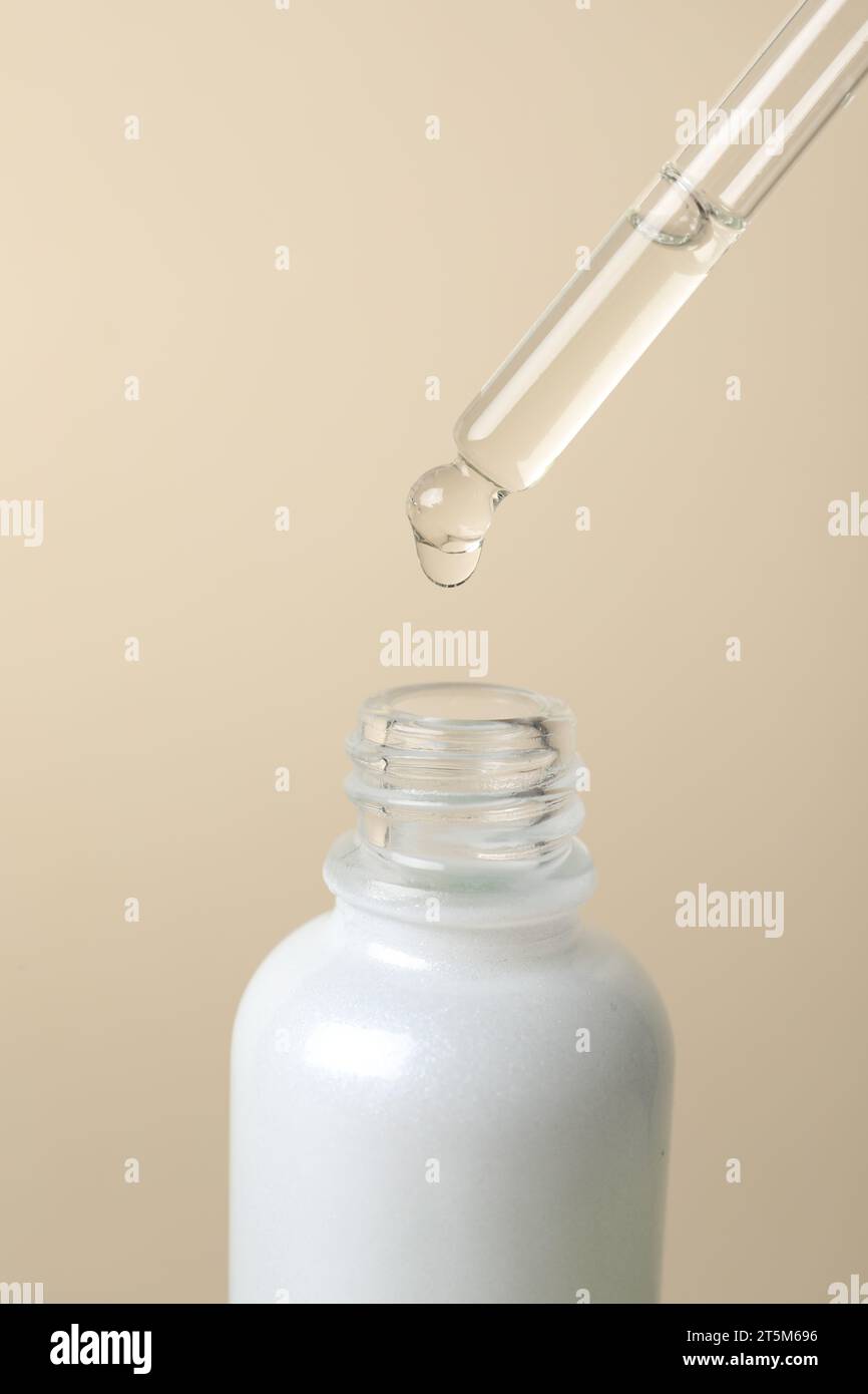 Dripping cosmetic serum from pipette into bottle on beige background ...