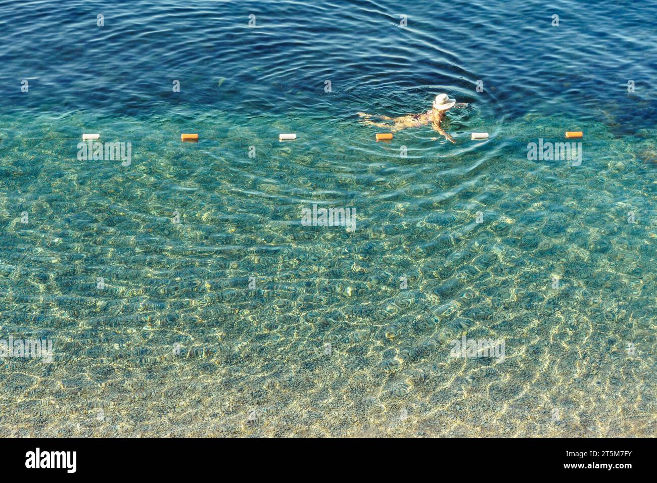 Woman in hat swims past colorful buoys in clear sea water. Lady enjoys ...