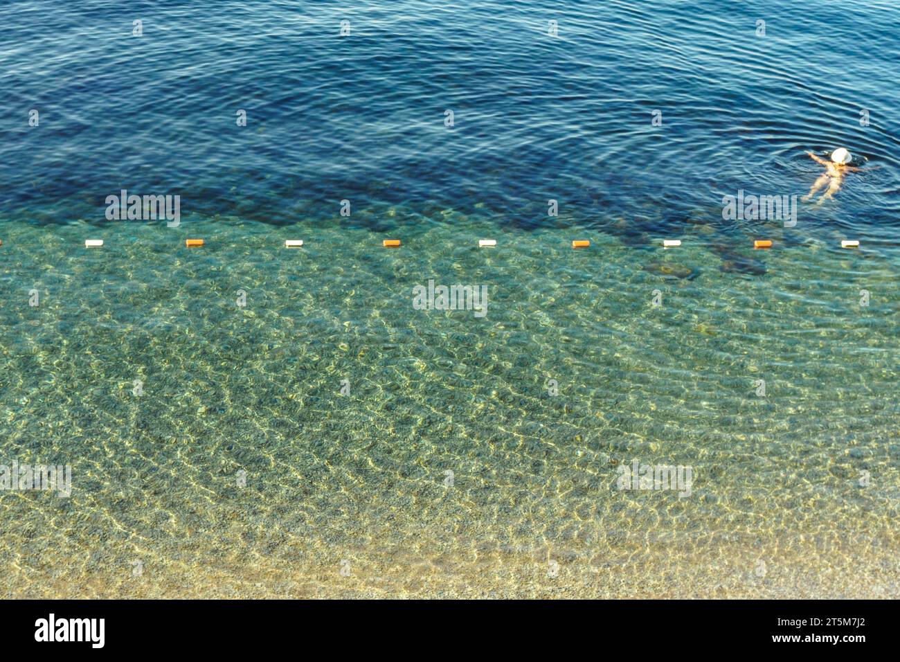 Woman in hat swims past colorful buoys in clear sea water. Lady enjoys ...