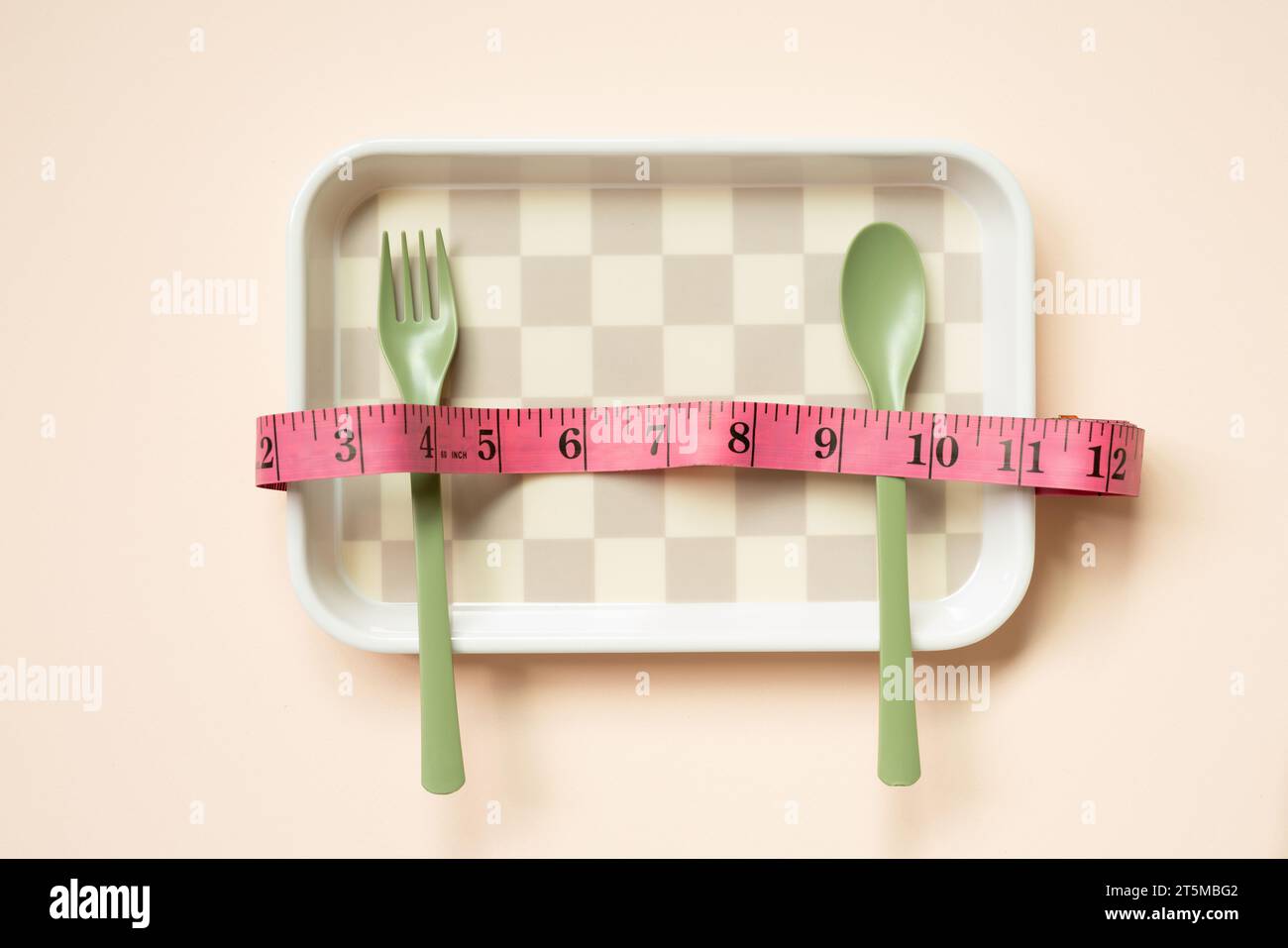 Empty tray plate and fork, spoon with tape measure on pink table ...
