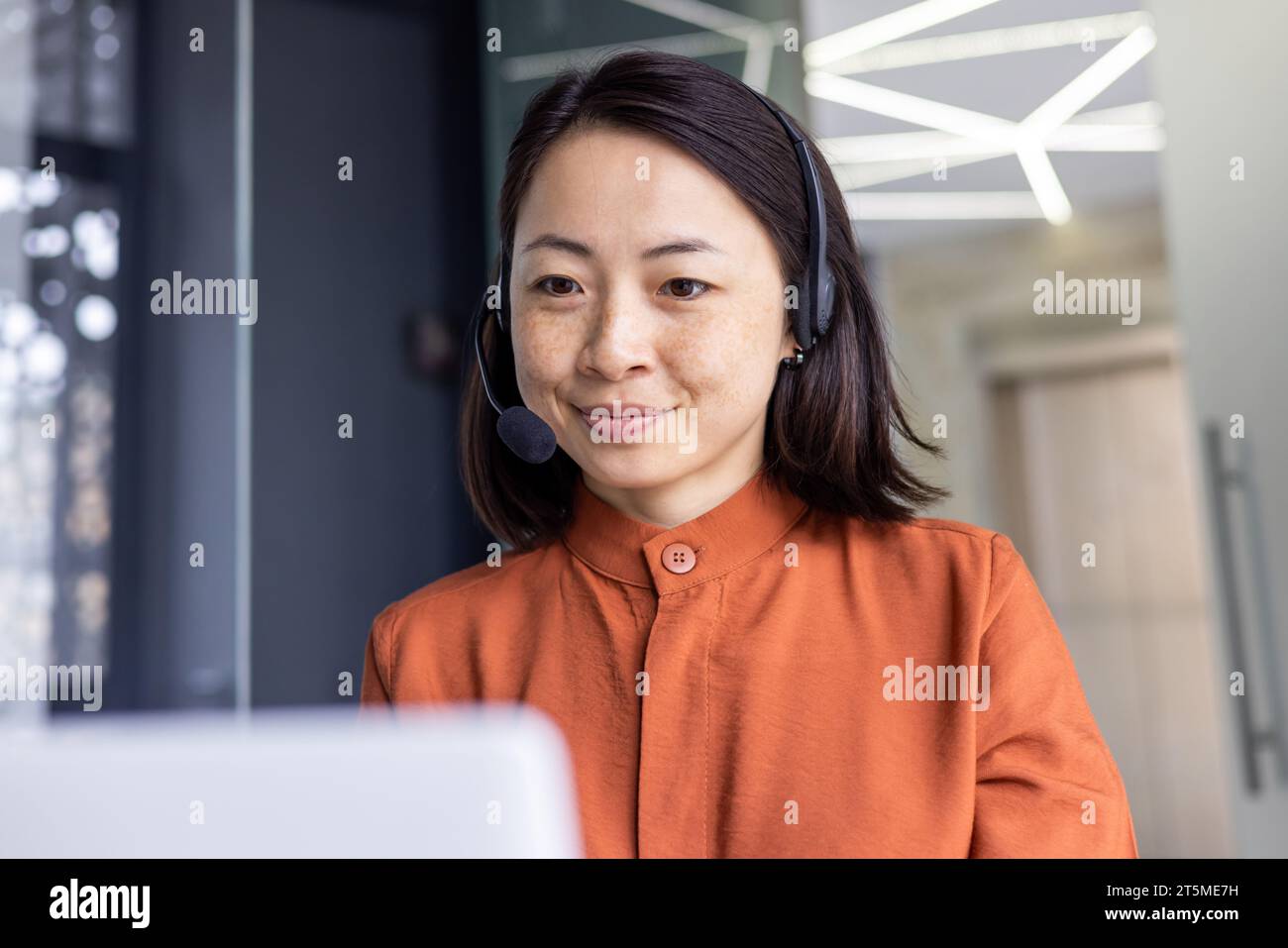 Serious Asian woman listening online conversation close up, businesswoman with headset phone ...