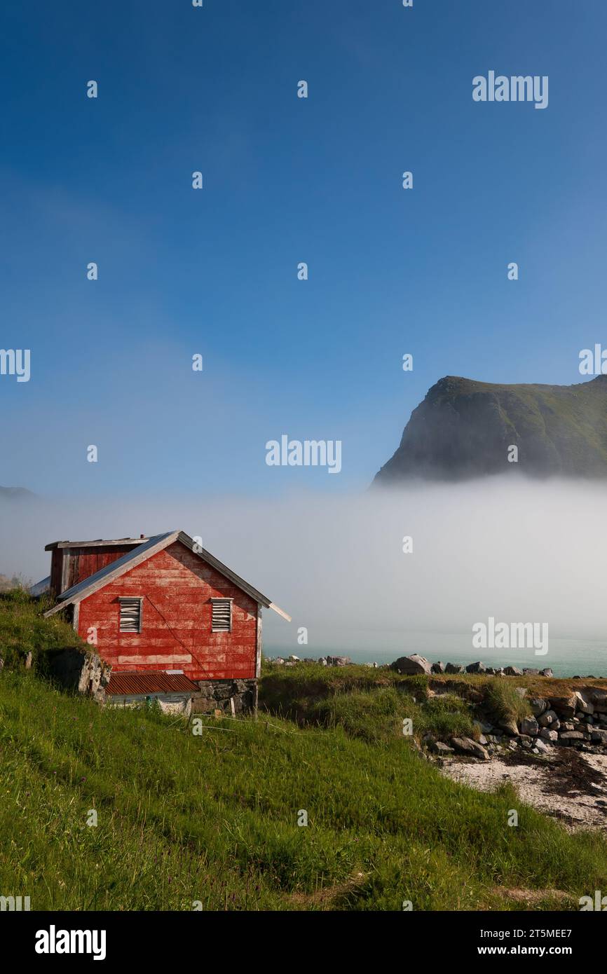 Red norwegian house in a fjord on a bright sunny morning, with fog ...