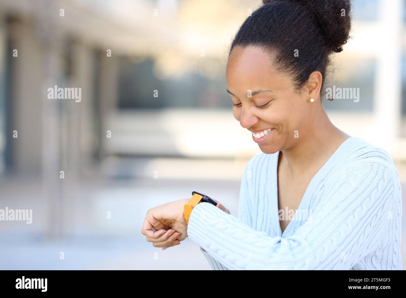 Black woman checking smartwatch smiling in the street Stock Photo - Alamy