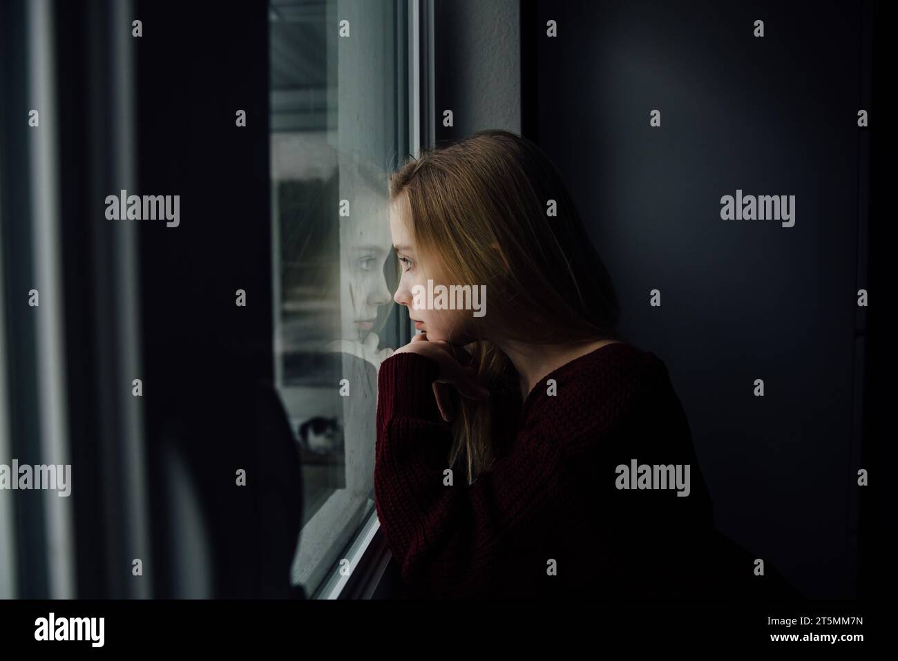 Serious preteen girl touches forehead to window with reflection Stock ...