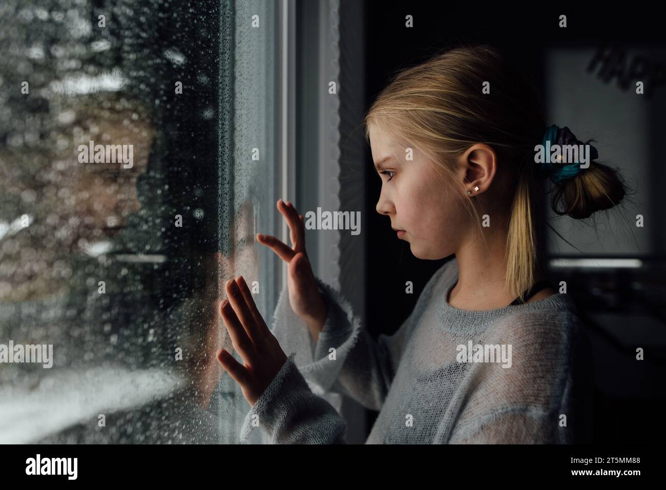 Girl looks seriously at hand while tracing fingertips on window Stock ...