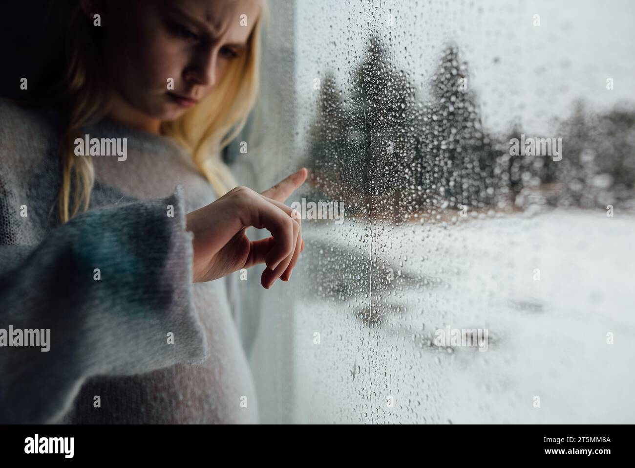 Young girl frowns while tracing finger over window with snow and Stock ...