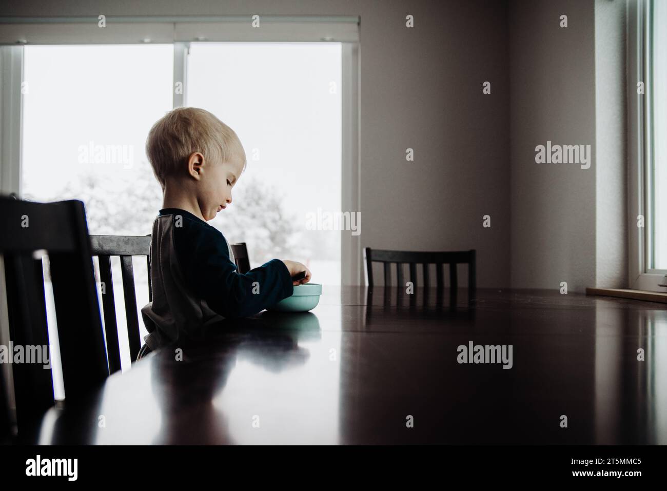Simple side view of little boy sitting at table at home eating f Stock ...