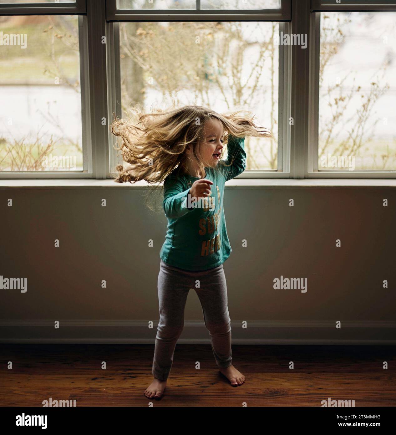 Happy little girl with long curls dancing in living room Stock Photo ...