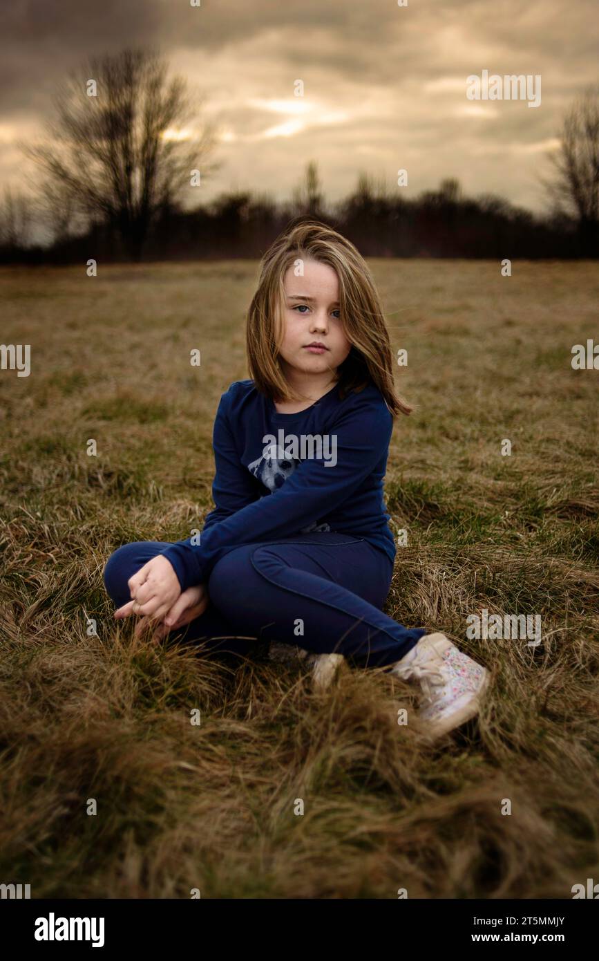 Beautiful young girl sitting in field at sunset Stock Photo - Alamy