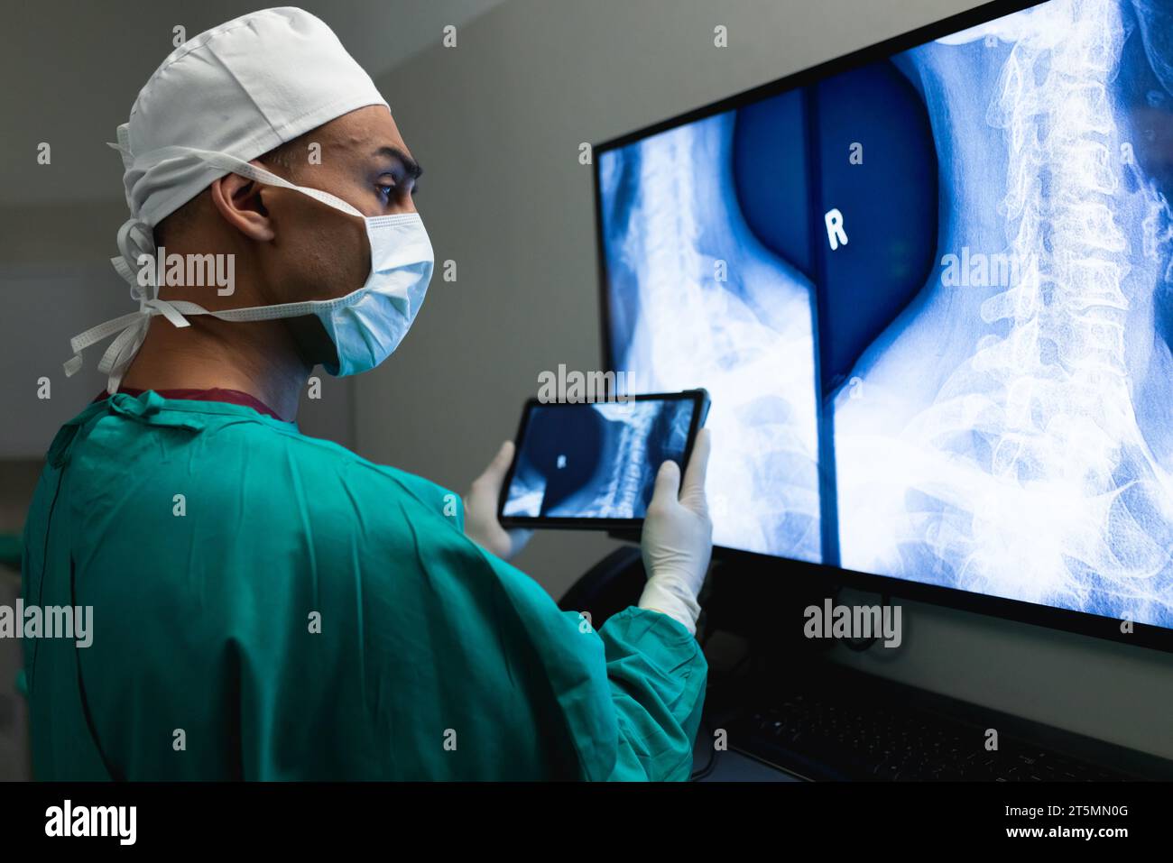 Biracial male surgeon looking at x-ray scans on screen in operating ...