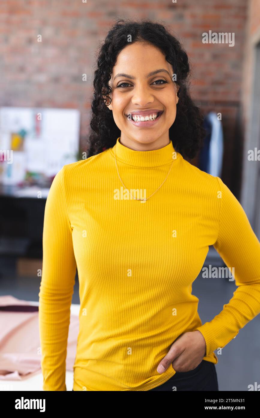 Happy biracial female fashion designer standing and smiling in sunny ...