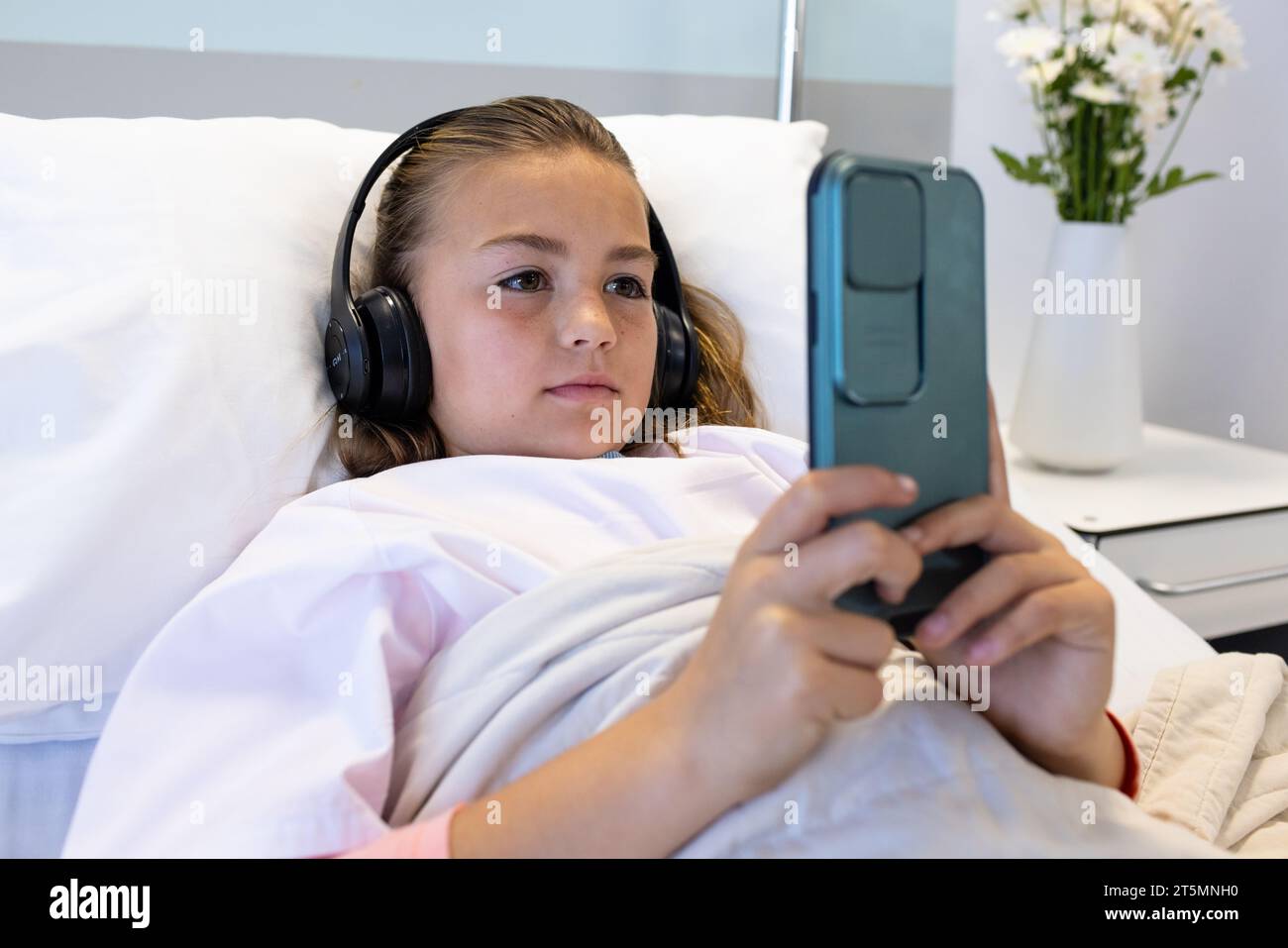 Caucasian girl patient lying in hospital bed wearing headphones using ...