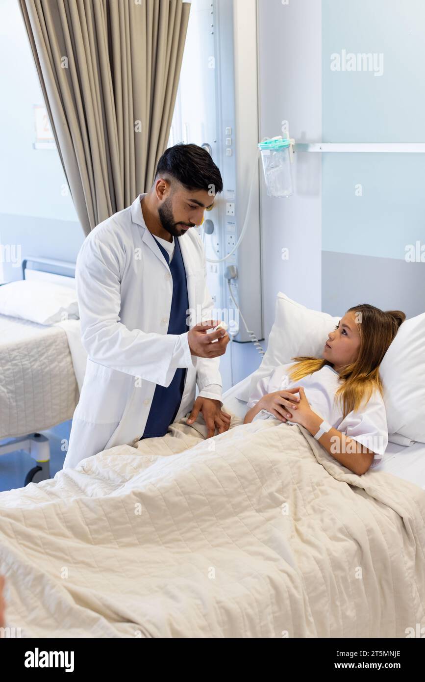 Diverse male doctor with asthma inhaler explaining to girl patient in ...