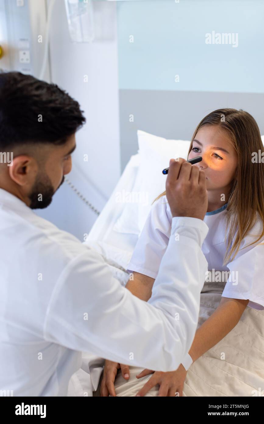Focused diverse male doctor checking eyes of girl patient with penlight ...