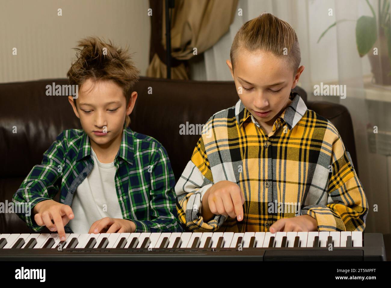 Two focused boys practice playing a piano duet in a cozy room Stock ...
