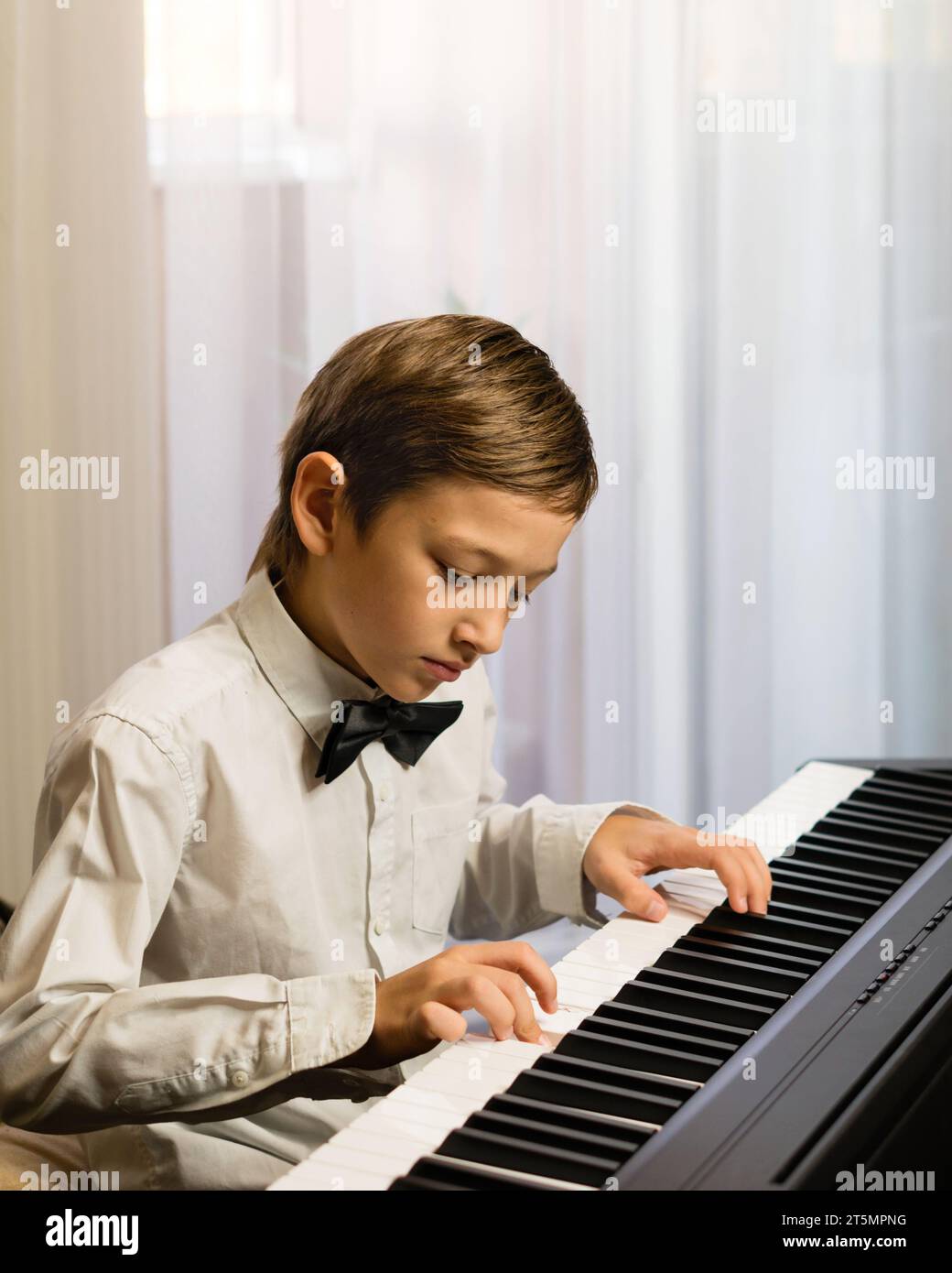 A young boy intently practices on a digital piano, dressed in formal ...