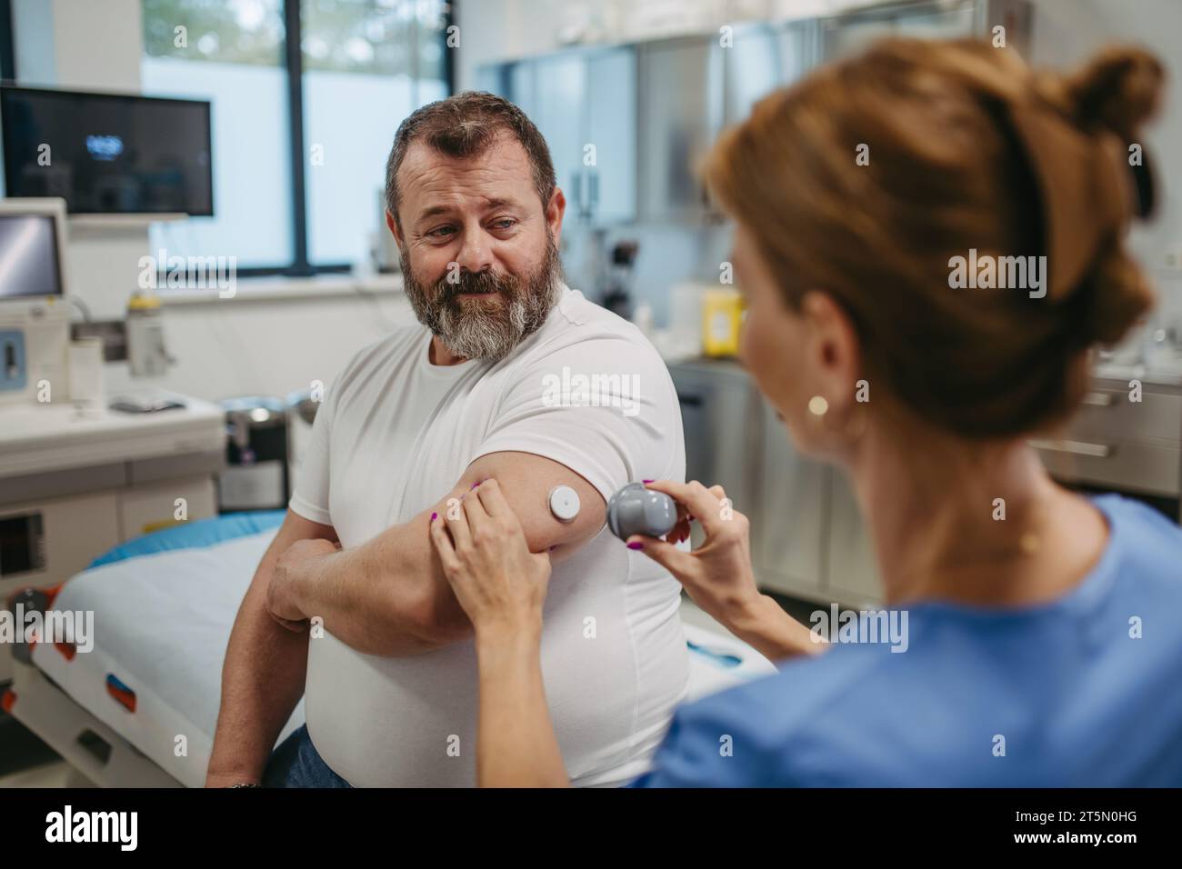 Doctor applying a continuous glucose monitor sensor on patient's arm ...